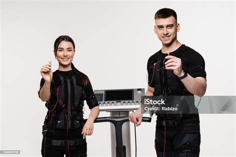 Ems를 입은 남자와 여자는 흰색 배경에 근육을 자극하기 위해 전기 충격을 사용하는 접촉기를 손에 들고 있습니다 전기 근육 자극 슈트를 입은 스포츠 그룹 훈련 18 19세에