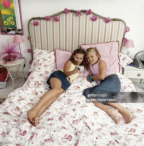 Two Girls Lying Side By Side On A Bed Photographing Themselves High Res