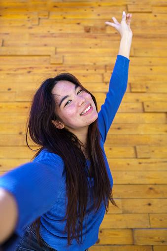 젊은 일본 여자가 평화 제스처를 만들고 나무 벽 배경으로 셀카를 찍는 모습 20 24세에 대한 스톡 사진 및 기타 이미지 20 24세 20 29세 Brand Name