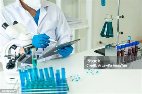 화학 실험실에서 현미경으로 액체 샘플을 검사하는 과학자와 함께 화학 실험실에서 Dna 분자를 검사하는 마스크 착용 의사 샘플을 다루는 연구원 Dna에 대한 스톡 사진 및