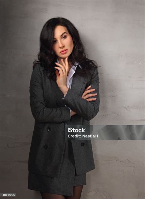 빈 복사 공간 로프트 스타일의 벽 스튜디오 배경에 접힌 팔에 서 있는 회색 사무실 양복과 치마에 심각한 사고 비즈니스 우먼 갈색 머리에 대한 스톡 사진 및 기타 이미지