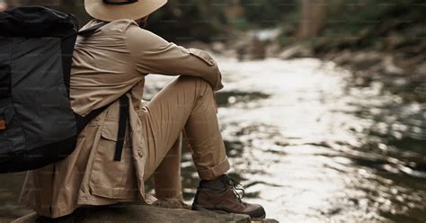 깊은 생각 배낭을 메고 모자를 쓰고 여행하는 동안 강 근처에 앉아 있는 청년 사진 Unsplash의 의류 이미지