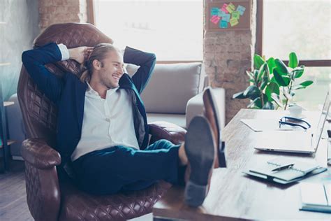 매력적인 웃는 행복 한 이사 직장에서 자신의 바탕 화면에 앉아 테이블에 다리를 퍼 팅 머리 뒤에 손을 잡고 휴식 시간을 즐기고 영화를 보고의 초상화 경영자에 대한 스톡 사진