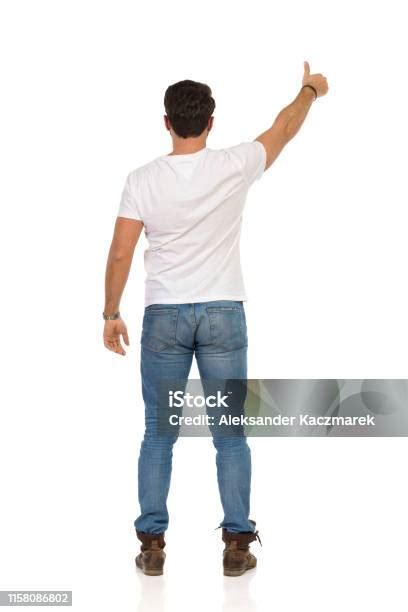 청바지와 흰색 티셔츠를 입은 청년이 팔을 들고 엄지손가락을 들고 서 있다 후면 보기 남자에 대한 스톡 사진 및 기타 이미지