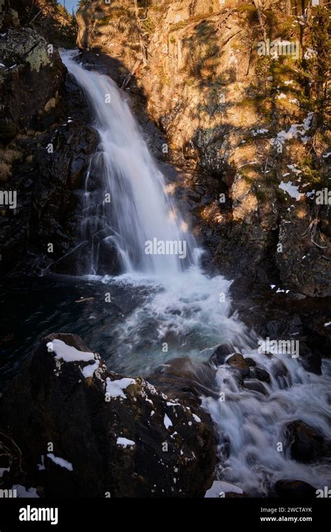 A Tranquil Waterfall Cascades Down A Rugged Terrain Surrounded By Forest With Snow Touched