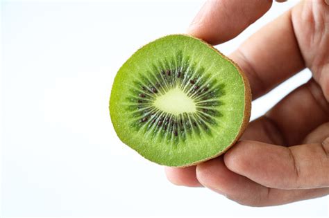 반으로 자른 키위 열매의 클로즈업 이미지 흐릿한 갈색 피부와 밝은 녹색 살 알아볼 수 없는 사람이 들고 있는 중국 구스베리 흰색 배경 전경에 초점 복사 공간 건강한 생활