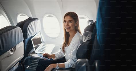 비행기 현창 옆에 앉아 있는 자신감 넘치는 여성 승객 앞에 노트북을 들고 스마트폰을 손에 들고 있다 사진 Unsplash의