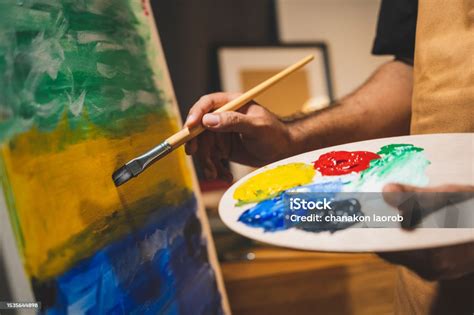 암실에 있는 아시아의 남자는 따뜻한 조명 예술가가 붓과 다양한 아크릴 색으로 그림을 그리는 작업을 하고 있다 예술 개념으로