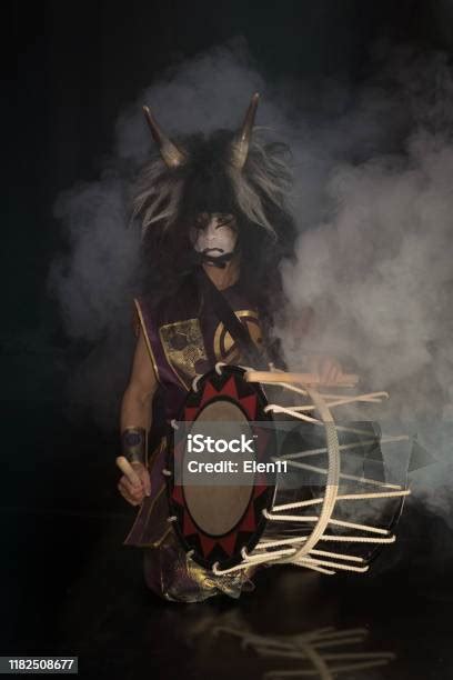 가발을 쓴 타이코 드러머와 무대 에서 악마 가면을 쓰고 드럼스틱과 드럼을 연기로 검은 배경에 두는 모습이 다 일본 신화에서 악마 Theatrical Performance에