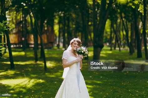 아름 다운 결혼식 Photosession입니다 흰 드레스와 베일 꽃과 화창한 날에 큰 녹색 공원에서 결혼식 산책에 나무 근처 리본 부케와 함께 아름 다운 Hairdress와