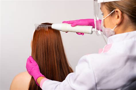 의료 용 마스크와 보호 화면을 착용한 미용사들은 긴 빨간 머리 소녀에게 Darsonval을 사용합니다 흰색에 건강한 머리 개념 2명에 대한 스톡 사진 및 기타 이미지