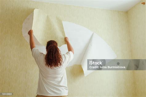 하얀 티셔츠 베이지 색 바지를 입고 의자에 서서 벽지에서 오래된 벽지를 찢어 버리는 Buxom 여성의 뒷모습 벽지에 대한 스톡 사진 및 기타 이미지 Istock