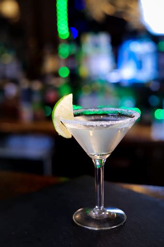 긴 줄기가 있는 깔때기 모양의 유리에서 알코올 칵테일은 불투명하고 불투명하며 유리의 설탕 가장자리에 라임 조각이 있습니다 보케의