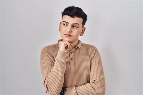 Non Binary Person Standing Over Isolated Background With Hand On Chin