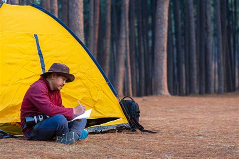 소나무 숲의 캠프장에서 텐트 옆에 앉아 자유 고독 야생으로의 평화로운 휴식 및 자연 치유 치료 개념에 대한 일기를 쓰면서 혼자 하룻밤 캠핑 40 44세에 대한 스톡 사진 및