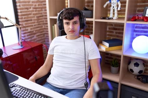 Non Binary Man Streamer Sitting On Table With Relaxed Expression At Gaming Room Stock Photo