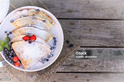 블루베리와 민트 잎을 얹은 팬케이크 숲 과일을 곁들인 큰 수제 팬케이크 흰 접시에 배경에 있는 납작하고 얇은 케이크 더미 복사 공간이 있는 나무 배경 건강한 생활방식에 대한