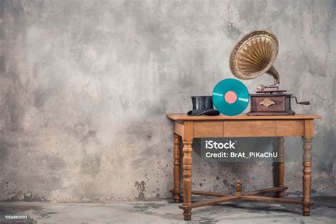 빈티지 황동 판 축음기 턴테이블 청록색 비닐 디스크 및 골동품 신사의 실린더 모자 나무 테이블 전면 콘크리트 벽 바탕에 세 레트로 오래 된 스타일 필터링 된 사진 1920