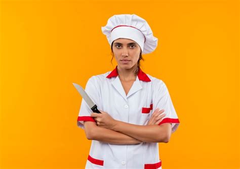 칼을 들고 복사 공간이 격리 된 노란색 벽에 손을 건너 요리사 유니폼을 입고 젊은 여성 요리사 무료 사진