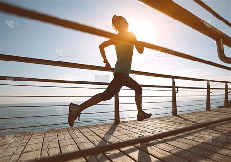 运动健身女性跑步在海滨木板路在日出