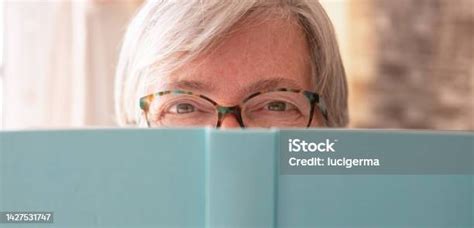 미소 짓는 카메라를 보는 책에 부분적으로 숨겨진 아름다운 백인 노인 여성의 초상화 은퇴를 즐기는 편안한 여성의 개념 70 79세에 대한 스톡 사진 및 기타 이미지 Istock