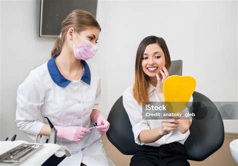 젊은 여성 치과 의사 치과 진료소에 치과 절차 후 거울에 자신의 이빨을 검사와 행복 한 여자 치과 개인 장식품에 대한 스톡 사진