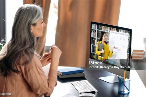 온라인 교육 비디오 콜을 통해 온라인으로 공부하는 중년 회색 머리 여성은 앱과 컴퓨터를 사용하여 작업 장책상에 앉아 온라인 수업을 듣고 플립 차트 근처의 교사가 화면에 들어