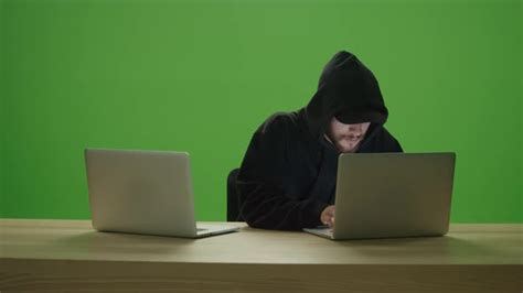 Unrecognizable Man Hacker Wearing Sweatshirt Hood And Cap Typing On 2 Laptops Technology Stock