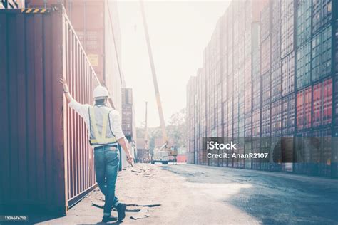 화물 컨테이너를 들고 서서 크레인을 보고 있는 엔지니어 감독관의 뒷모습 작업 현장에서 관찰 작업 활동 손 홀드 무전기는 반사 천과 단단한 모자를 착용합니다 항만 근로자에