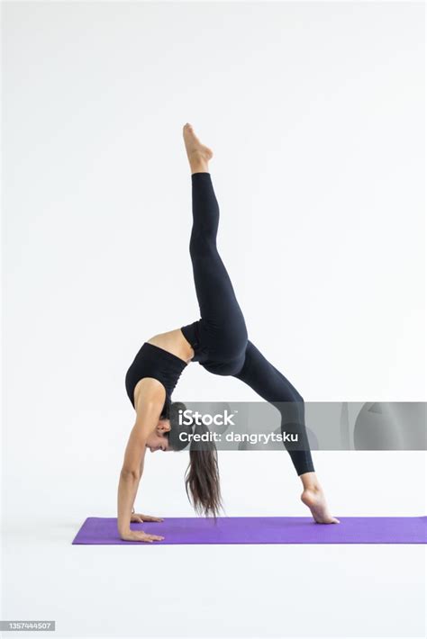 젊은 매력적인 여자 연습 요가 다리 운동에 서 한 다리 바퀴 포즈 스포츠웨어를 입고 운동 흰색 바지 실내 전체 길이 흰색 배경에