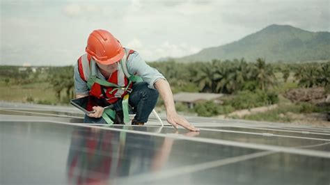 클로즈업 높이에서 떨어지는 것을 방지하기 위해 안전 장비를 착용 한 엔지니어 또는 기술자 또는 계약자는 지붕의 태블릿에있는 응용 프로그램을 통해 전기를 생산하기 위해 태양