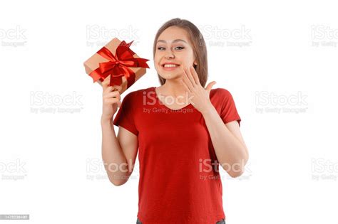 빨간 티셔츠를 입은 행복한 미소 짓는 소녀의 초상화가 선물 상자를 들고 흰색 배경 위에 포즈를 취하고 있다 긴 머리 미소 웃음과 기쁨으로 보이는 쾌활한 갈색 머리 여자 20