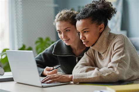 Premium Photo Two Young Colleagues Sitting At Table In Front Of Laptop And Looking At Screen