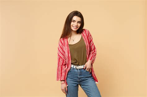 스튜디오에서 파스텔 베이 지 배경에 고립 된 주머니에 손을 잡고 카메라를 찾고 캐주얼 옷에 웃는 젊은 여자의 초상화 사람들은 진심으로 감정 라이프 스타일 개념입니다 복사