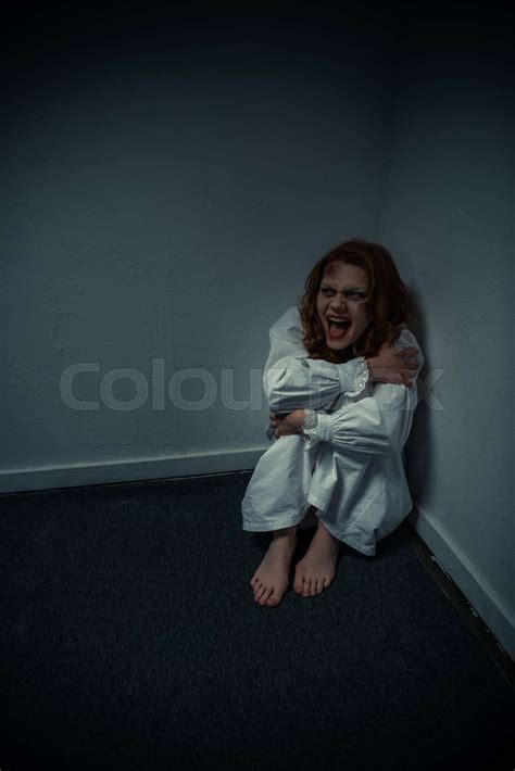 Evil Girl In Nightgown Shouting And Sitting Near Wall Stock Image