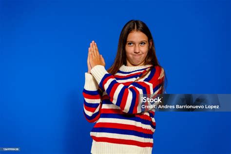 파란색 배경에 줄무늬 스웨터를 입은 아름다운 히스패닉 소녀는 용서를 구하면서 후회스러운 표정으로 손바닥을 함께 내다봅니다 제발 실례합니다 사람들에 대한 스톡 사진 및 기타