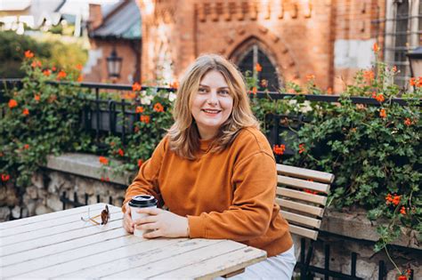 바이오 커피 종이컵을 들고 웃는 여자 그녀는 도시 거리의 카페 테라스에 앉아 있습니다 도시 개념 행복한 30 대 소녀 야외에서 커피와 함께 테이블에 앉아있는 금발 머리에