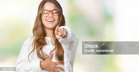 격리 된 이상 안경 및 겨울 모자를 입고 젊은 아름 다운 갈색 머리 Hipster 여자 배경 당신의 가슴 부 끄 러운 식 위에 손가락 손으로 카메라를 가리키는 웃음