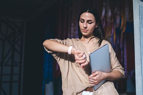 도시 환경에서 원격 동료를 기다리는 동안 웨어러블 스마트 워치에서 시간을 확인하는 현대 휴대용 컴퓨터를 가진 백인 여성 가젯 디스플레이를보고있는 젊은 여성 프리랜서 Z세대에