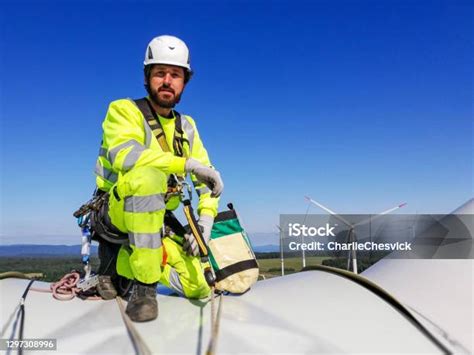 산업용 등산가 로프 액세스 기술자가 거대한 육상 풍력 터빈에 무릎을 꿇고 풍력 발전 단지와 블레이드 검사를 준비하고 카메라를