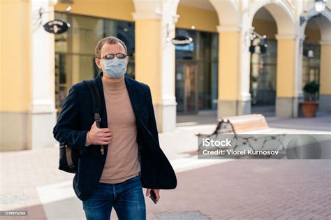 코로나바이러스와 전염병이 있는 동안 유럽 남자는 보호 용 얼굴 마스크를 착용하고 배낭을 운반하고 버스 정류장에서 야외에서 포즈를