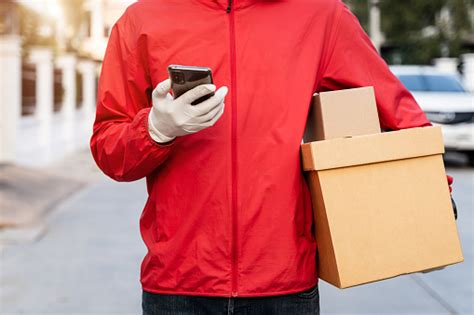 빨간 유니폼을 입은 배달남자의 자른 샷은 거리에서 우편 소포 스탠드를 들고 고객에게 물건을 전달하기 위해 Gps 주소를 확인하는