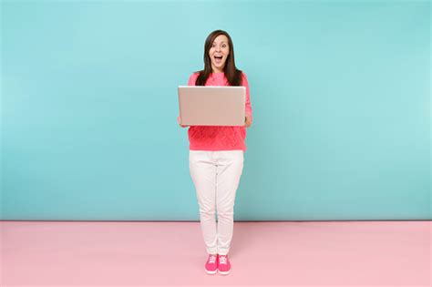 장미 니트 스웨터 노트북 Pc 컴퓨터를 사용 하 여 흰 바지에에서 여자의 전체 길이 초상화 스튜디오에서 밝은 핑크 블루 파스텔 벽 배경에 고립 패션 라이프 스타일 개념입니다