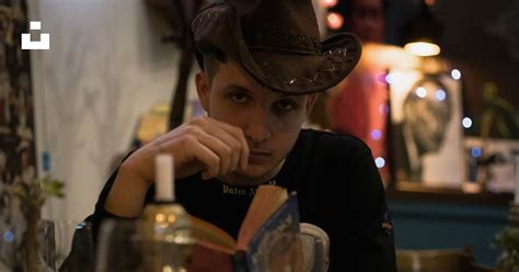 검은색 카우보이 모자를 쓰고 검은색 긴팔 셔츠를 입은 남자가 와인 잔이 있는 테이블 옆에 앉아 있다 사진 Unsplash의 무료 의복 이미지