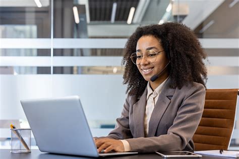 양복을 입고 책상에 앉아 사무실에서 노트북으로 작업하는 미소 짓는 젊은 아프리카계 미국인 비즈니스 여성 검사 보기에 대한 스톡 사진 및 기타 이미지 Istock