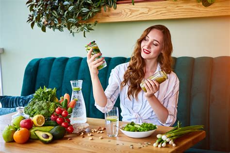 배경에 녹색 꽃과 신선한 과일과 야채와 아름다운 인테리어에 스무디와 신선한 물을 마시는 젊은 여성 건강한 식생활 개념 비건 식사