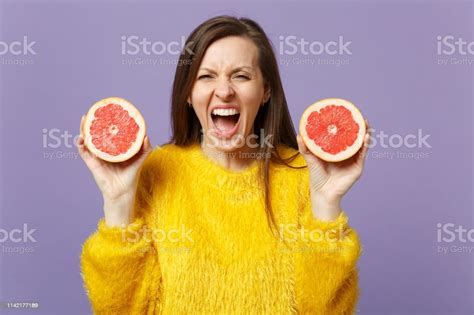 스튜디오에서 보라색 파스텔 배경에 고립 된 신선한 익은 자 몽의 Halfs를 들고 모피 스웨터에 미친 비명 젊은 여자 사람들은 생생한 라이프 스타일 휴식 휴가 개념입니다