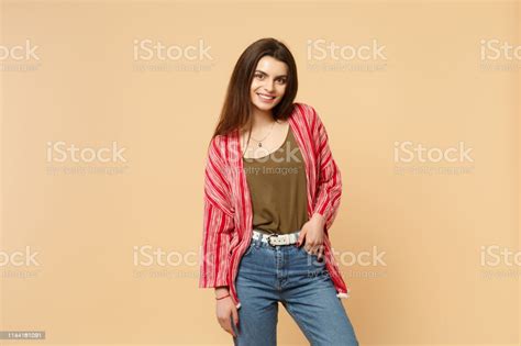 스튜디오에서 파스텔 베이 지 배경에 고립 된 주머니에 손을 잡고 카메라를 찾고 캐주얼 옷에 웃는 젊은 여자의 초상화 사람들은 진심으로 감정 라이프 스타일 개념입니다 복사