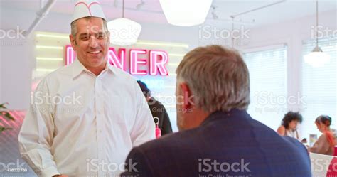 흰색 버튼 다운 셔츠와 종이 모자를 쓴 남자가 1950년대 스타일의 식당에서 고객과 이야기하는 어깨 너머로 찍은 사진 20 24세에 대한 스톡 사진 및 기타 이미지 Istock