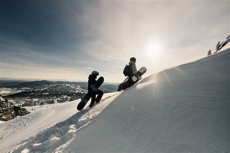 겨울 산에서 프리라이드를 위해 깊은 눈 경사로로 걷는 보드를 들고 있는 스노우보더의 실루엣 커플 눈 덮인 절벽과 나무 2명에 대한 스톡 사진 및 기타 이미지 Istock